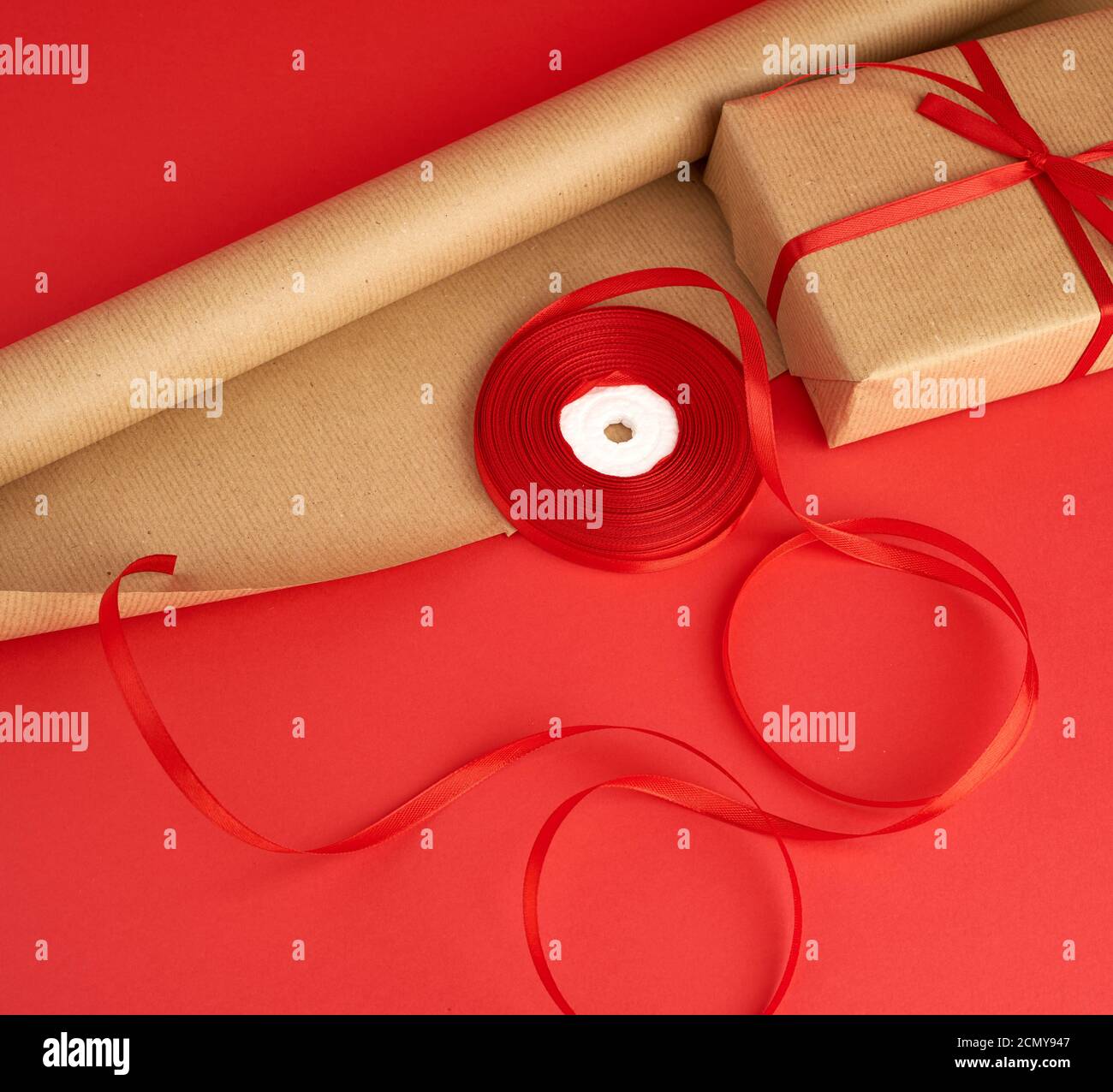paper for packaging, a reel of red ribbon and a wrapped gift in brown ...