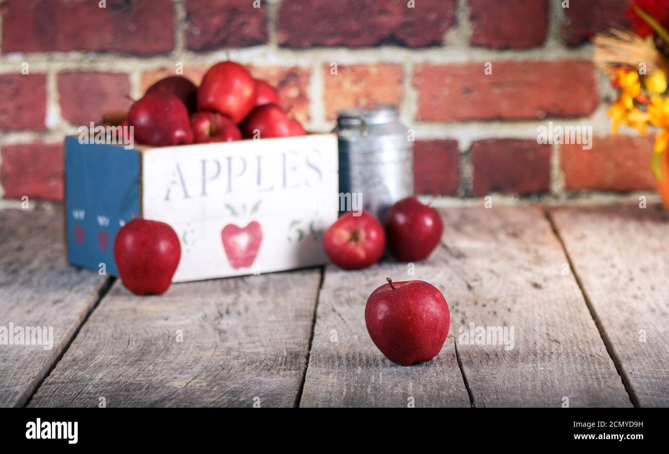 Red Apples in a box and scattered on a wood floor in front of a brick ...