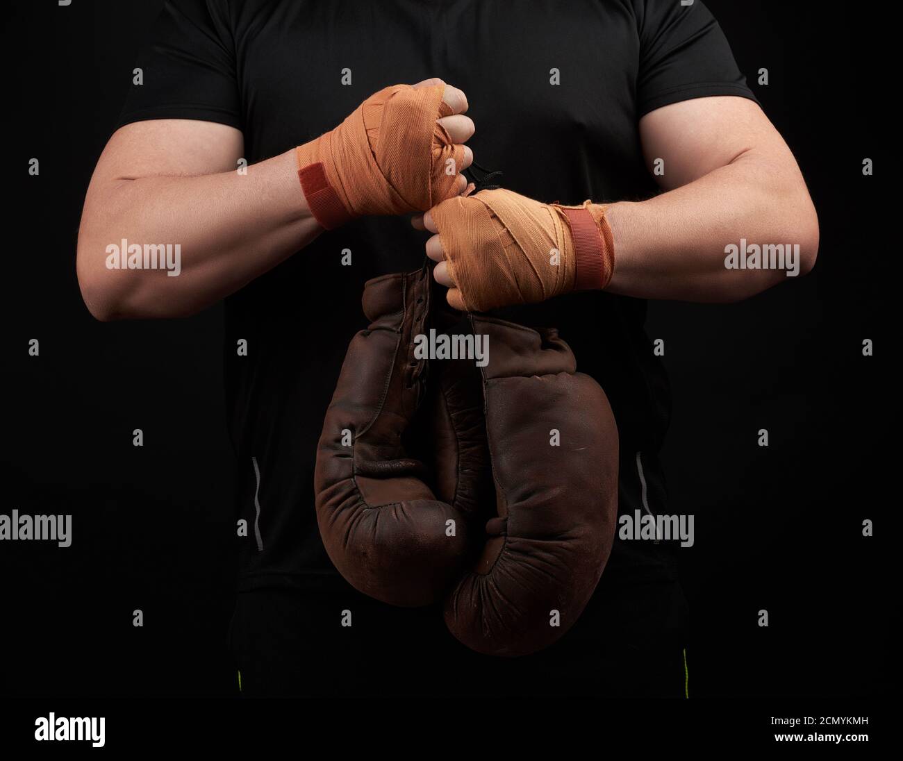 muscular athlete in a black uniform holds very old brown boxing gloves ...