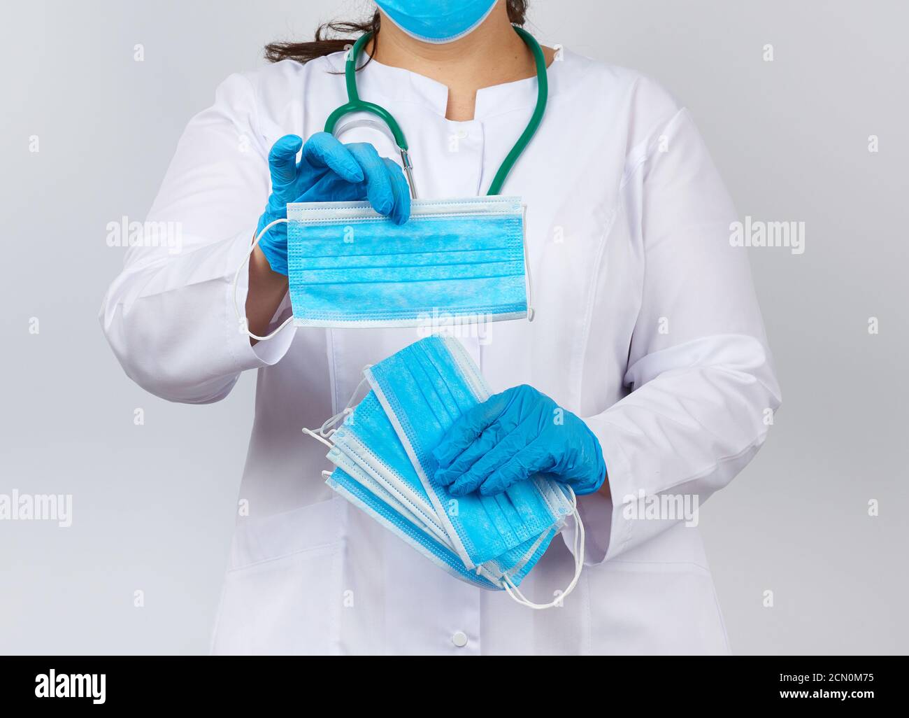female doctor in a white coat and mask holds a stack of protective face ...