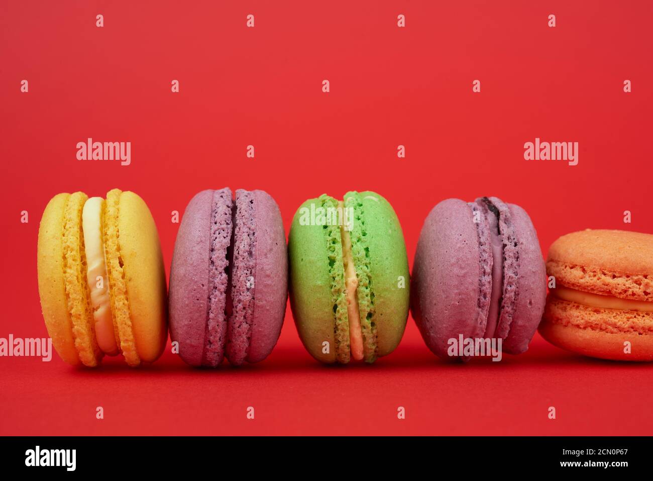 yellow, purple, green round baked macarons cakes on a red background ...