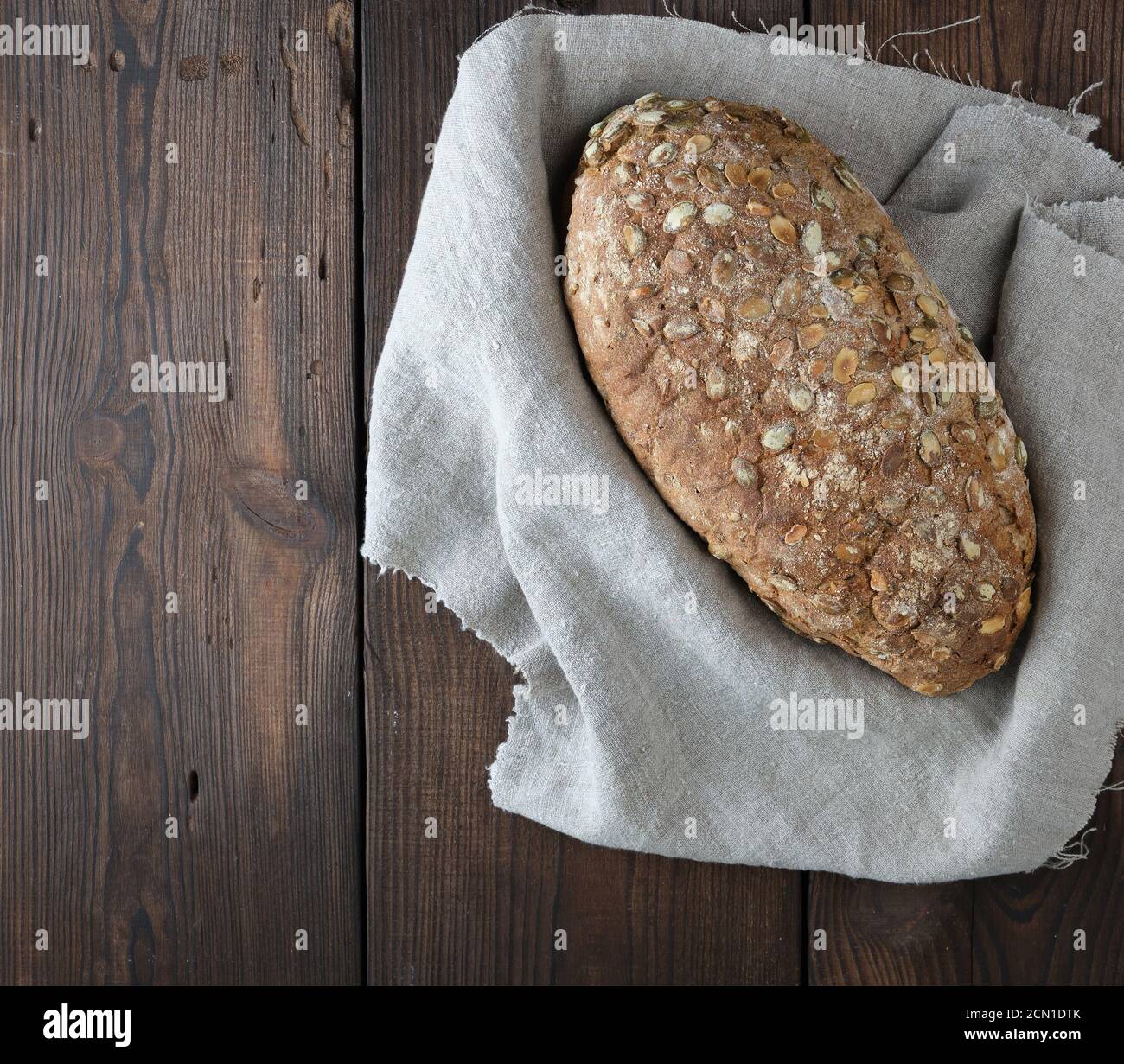 baked oval bread made from rye flour with pumpkin seeds on a gray linen ...