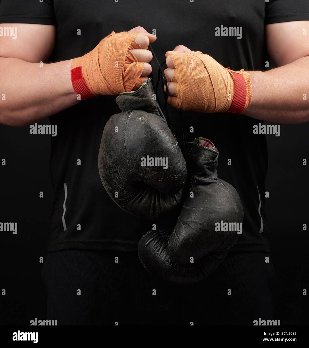 muscular athlete in a black uniform holds very old black boxing gloves ...
