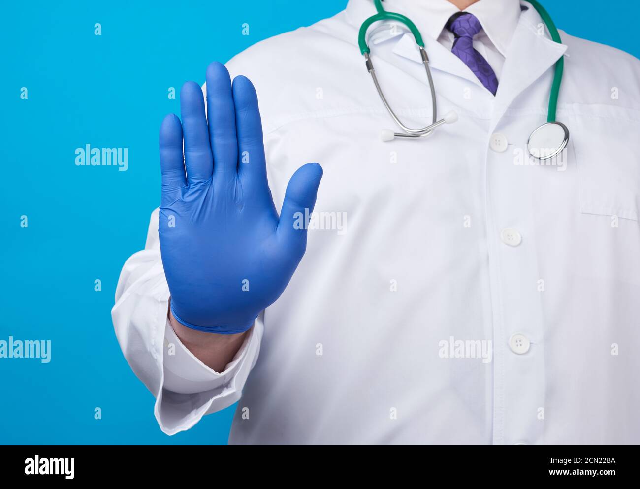male doctor in a white coat and blue sterile gloves shows a stop ...