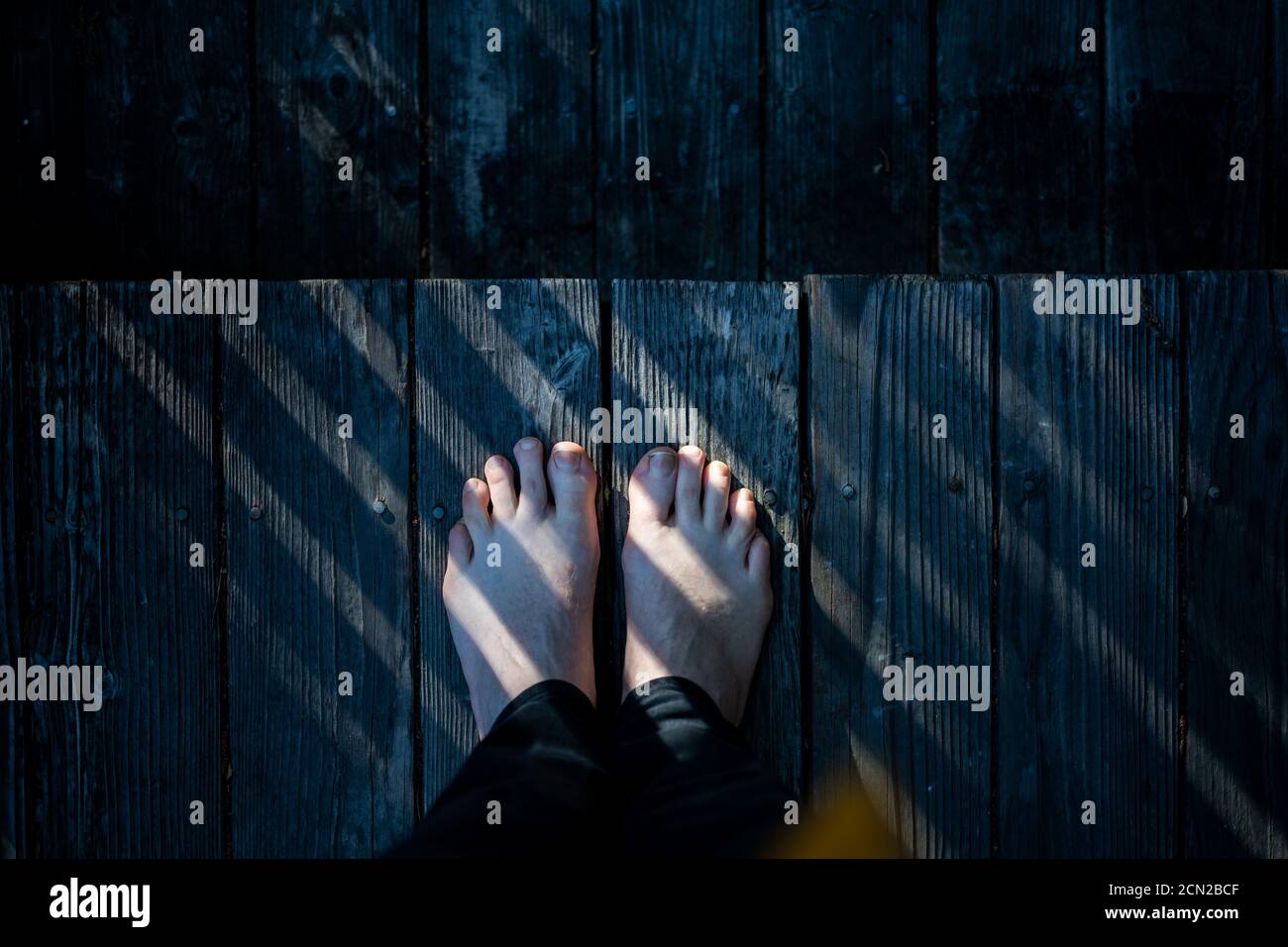 Looking down on bare feet standing on wood deck with lines of light ...