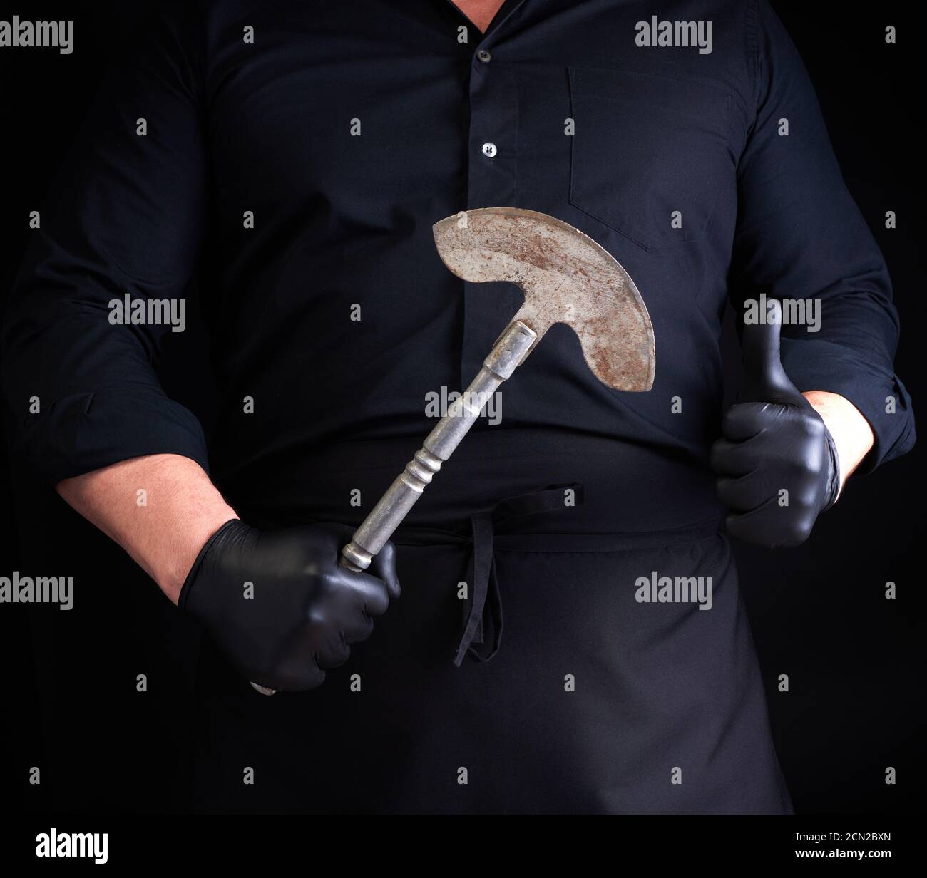 man in black clothes, latex gloves holds a vintage metal ax-knife for ...