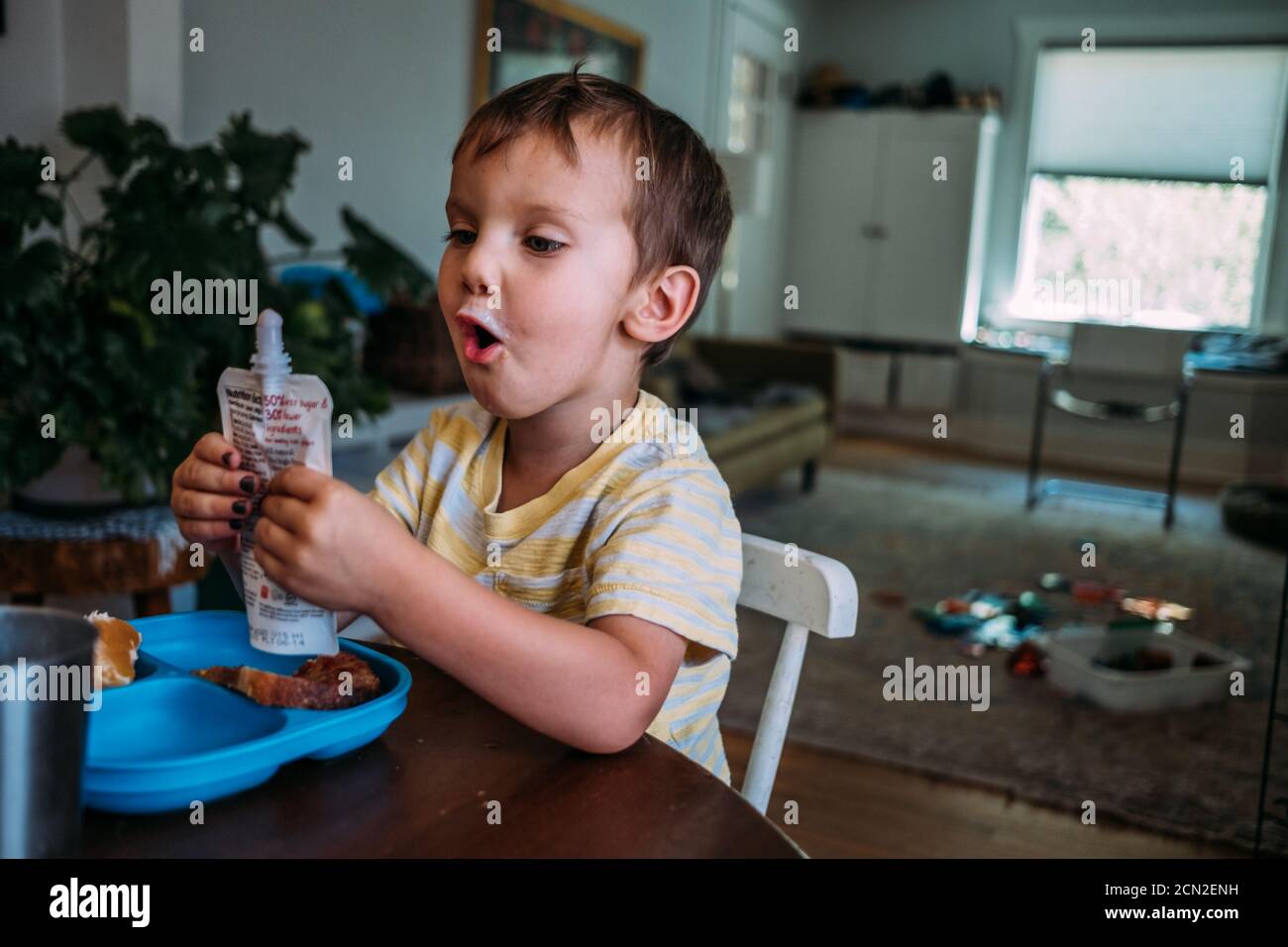 Young child excited about a squeeze yogurt at the table Stock Photo - Alamy