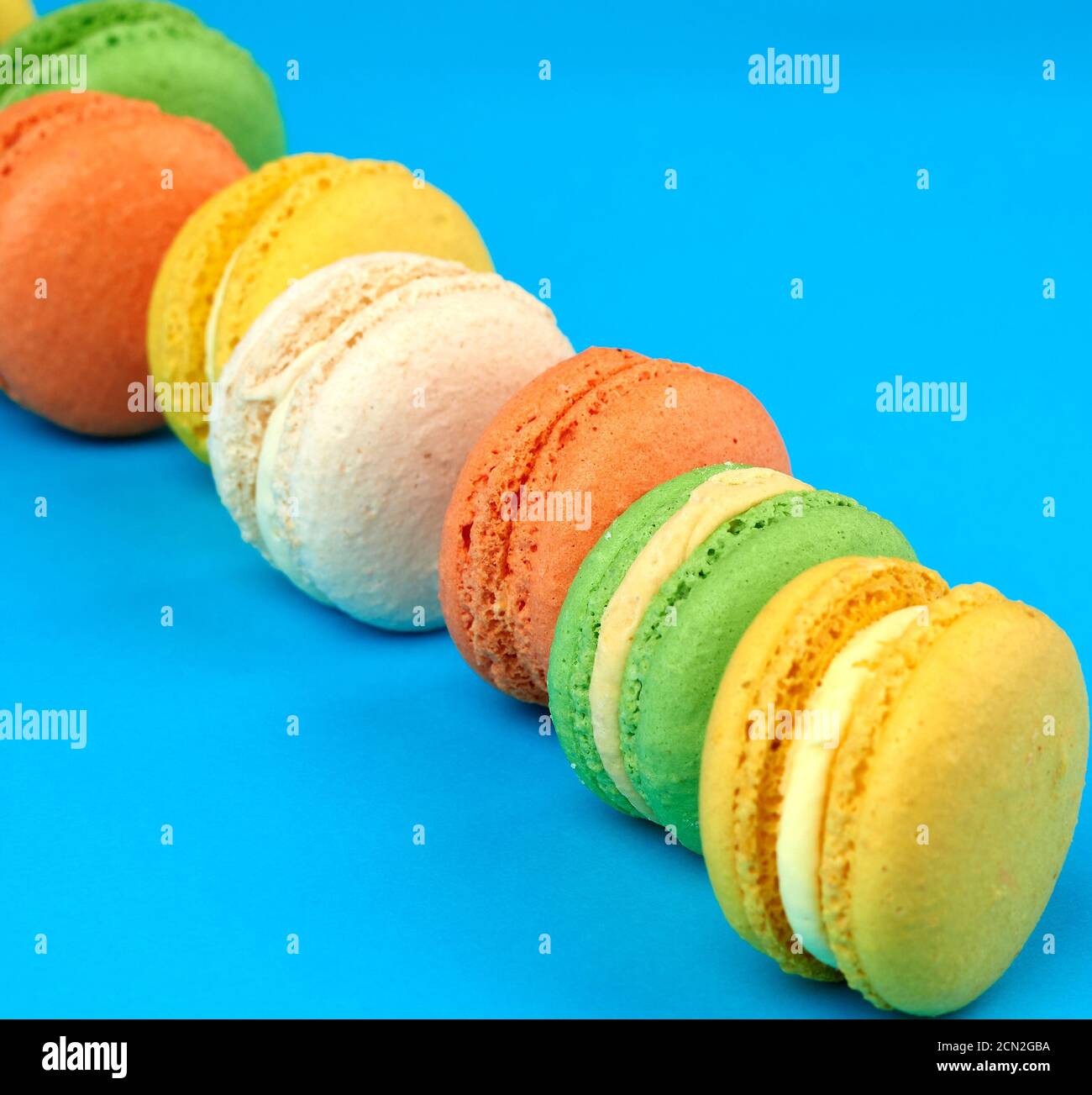 round multi-colored baked macarons with cream lie in a line on a blue ...