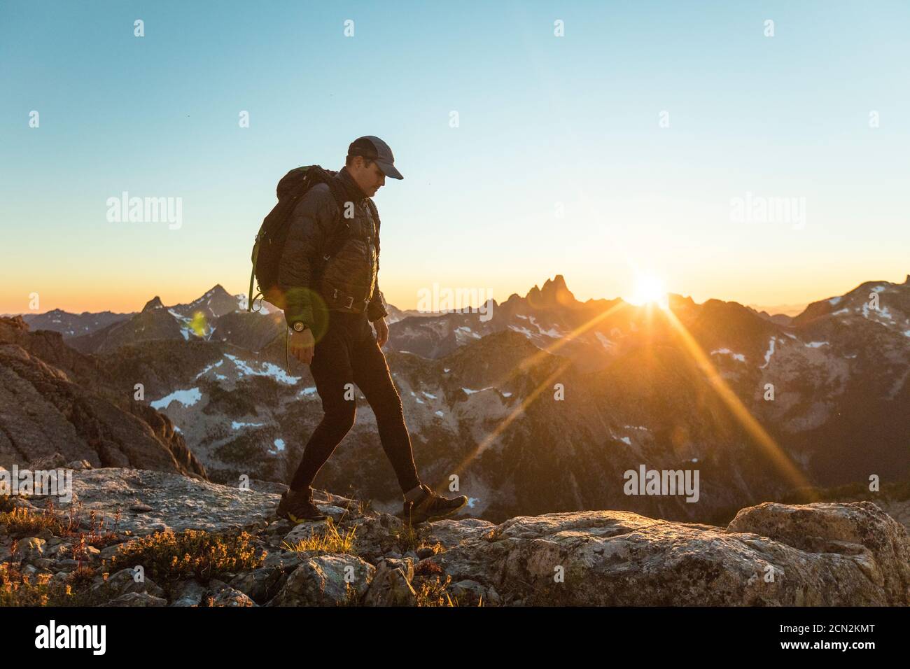 Adventurous man hiking along mountain ridge during sunset Stock Photo ...