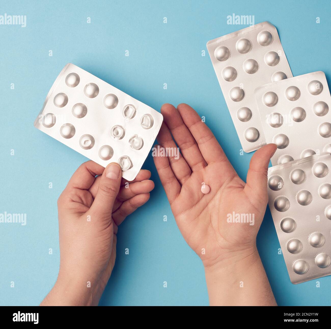 two hands hold a package of round tablets in blister packs, blue ...
