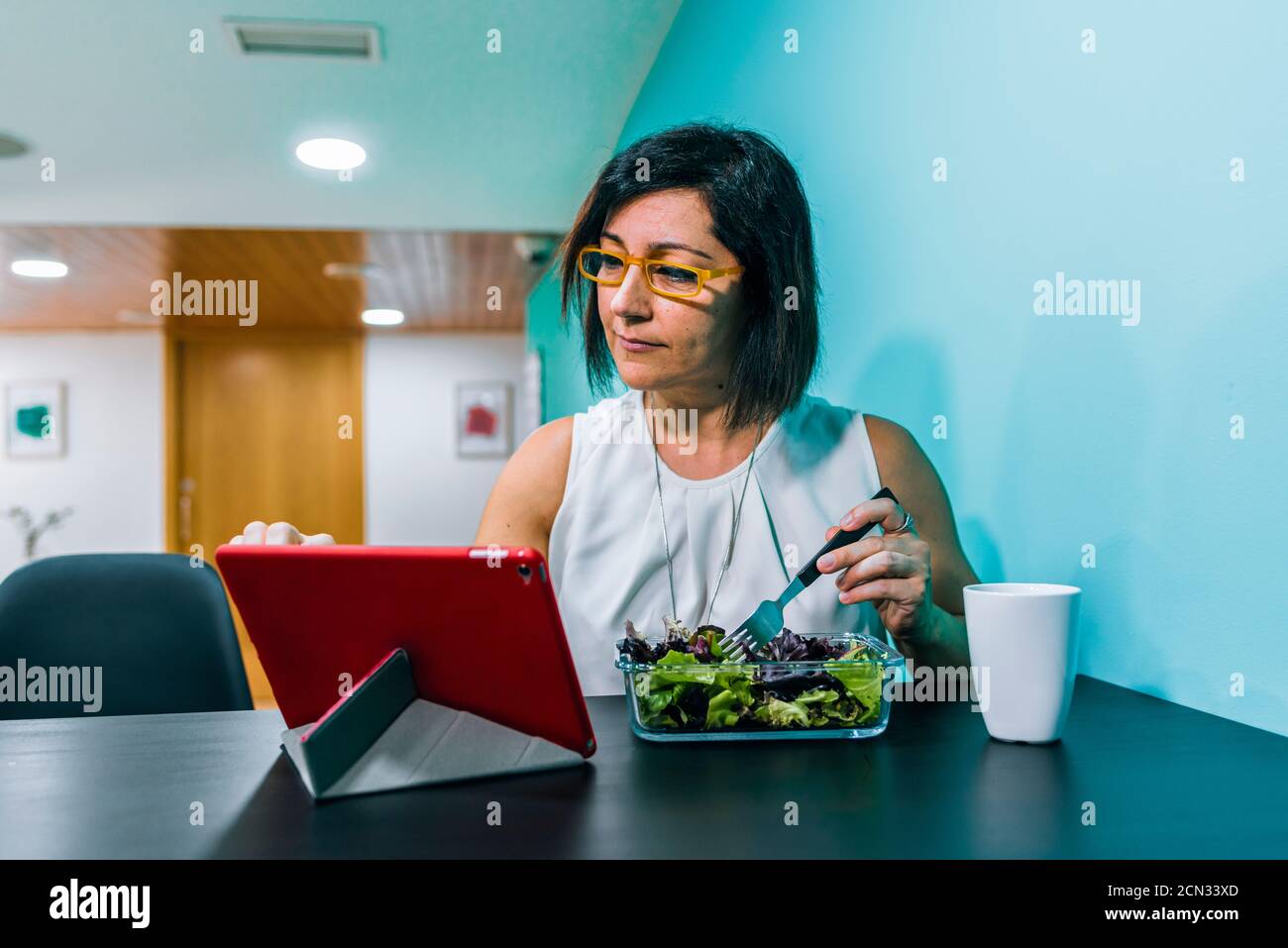 A woman using a tablet while eating healthy food. Coworking concept ...