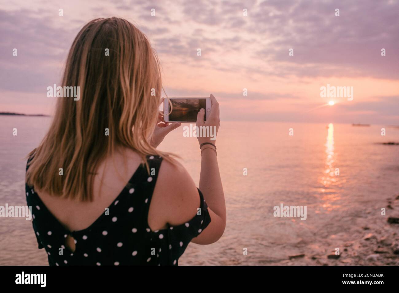 Back view of young woman taking a photo of sunset Stock Photo - Alamy