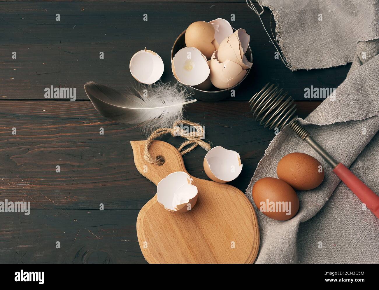 brown raw chicken eggs, shells, cutting board and hand-held whisk for ...