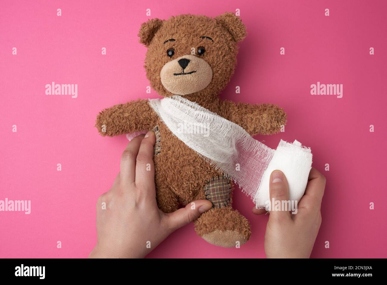 brown teddy bear with bandaged torso with white gauze bandage on a pink ...