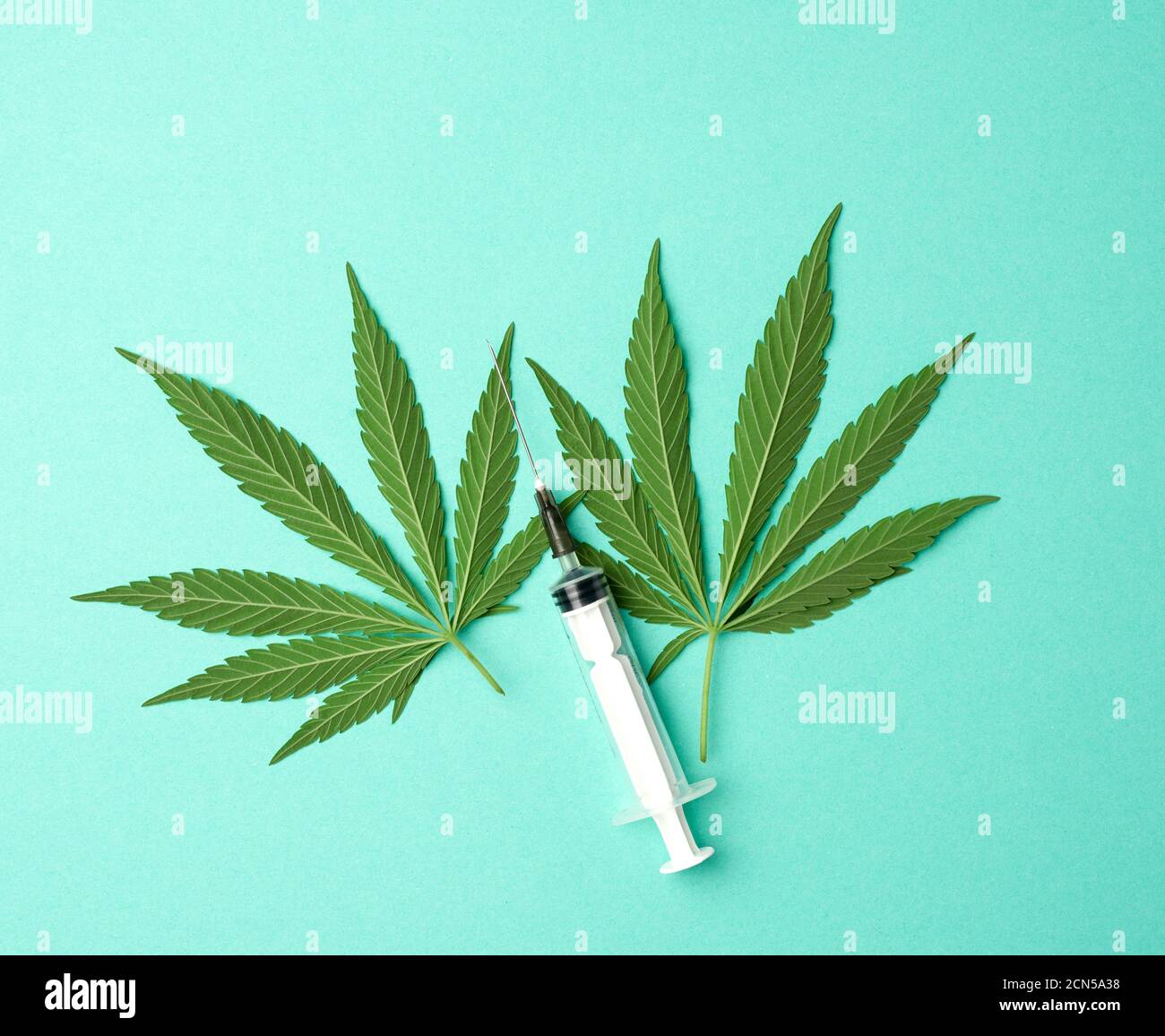 Plastic Syringe With A Needle And Green Leaves Of Hemp On A Blue