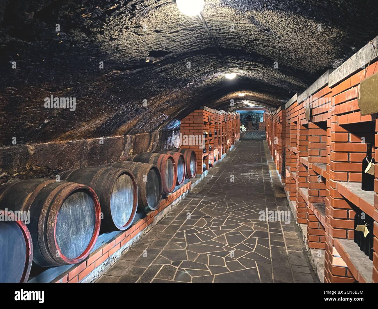 Old local winery - wine bottles and barrels on stone bricks shelves ...