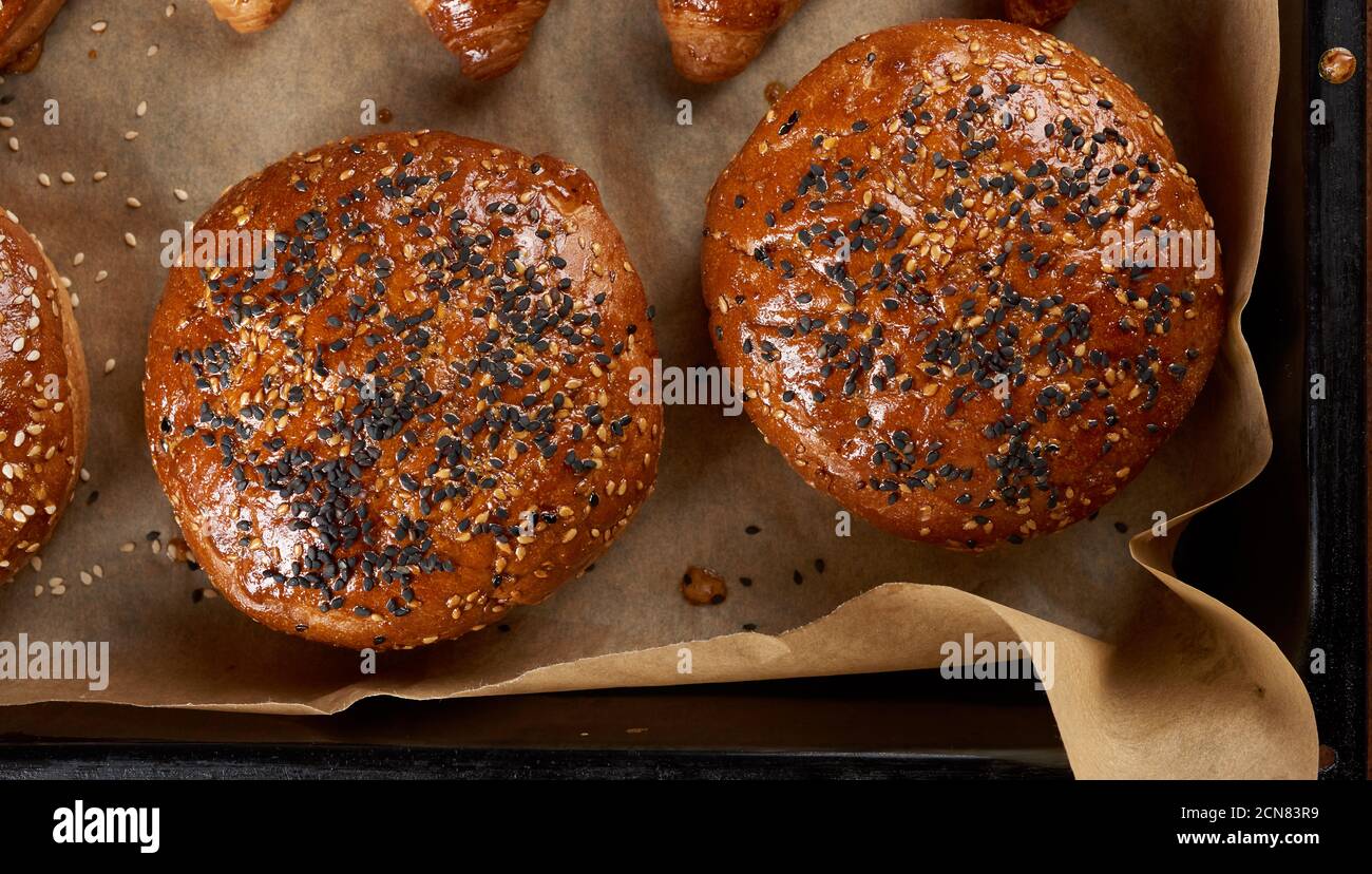 baked sesame buns on brown parchment paper, ingredient for a hamburger ...