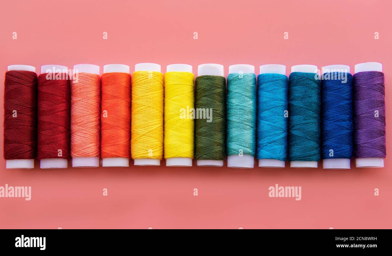 Spools of thread on the colors of the rainbow on a pink background ...