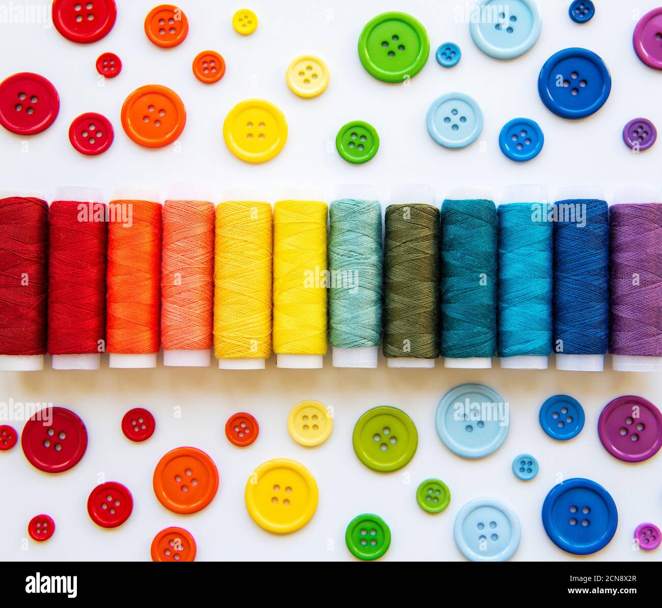 Spools of thread and buttons on the colors of the rainbow on a white ...