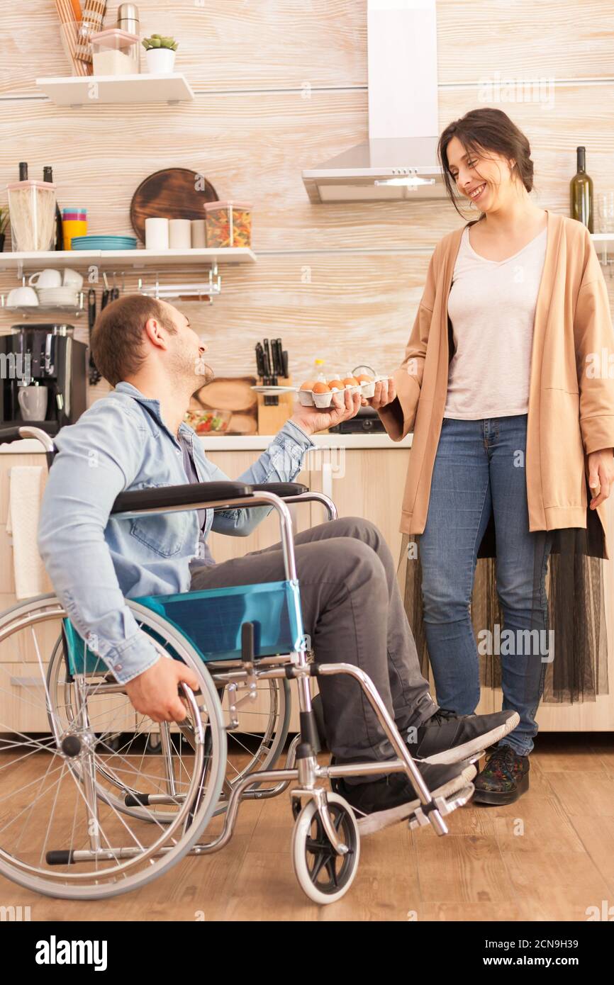 Disabled man in wheelchair holding eggs box for his wife in kitchen ...