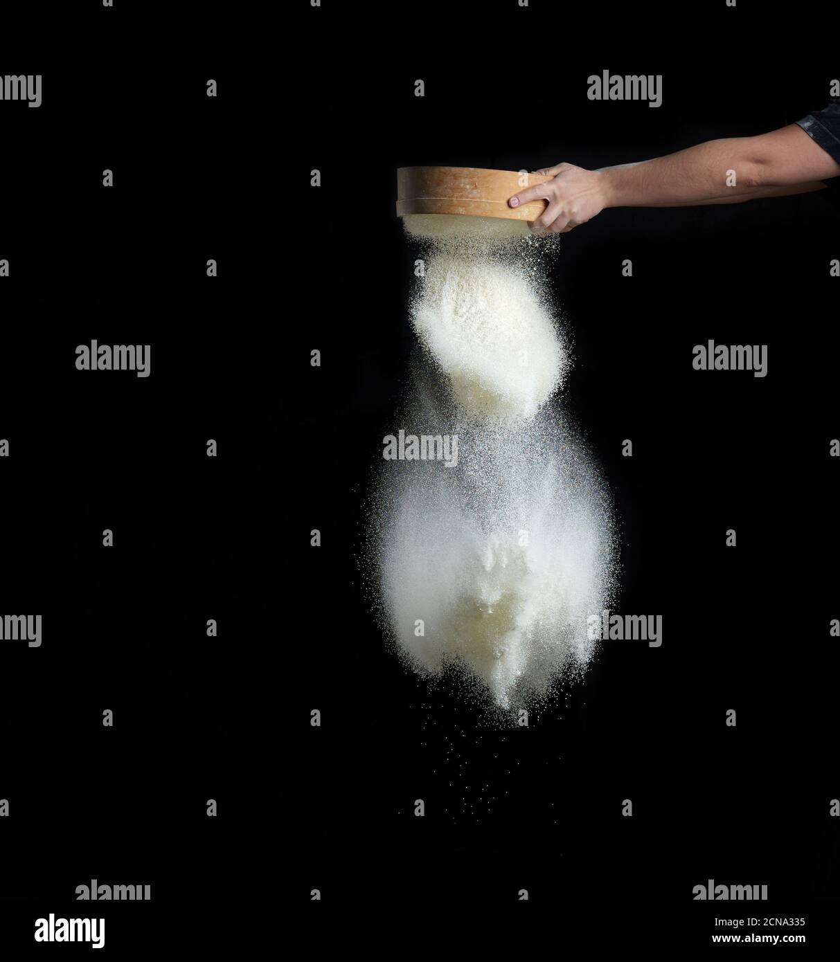 female hand sifts white wheat flour through a round wooden sieve on a ...