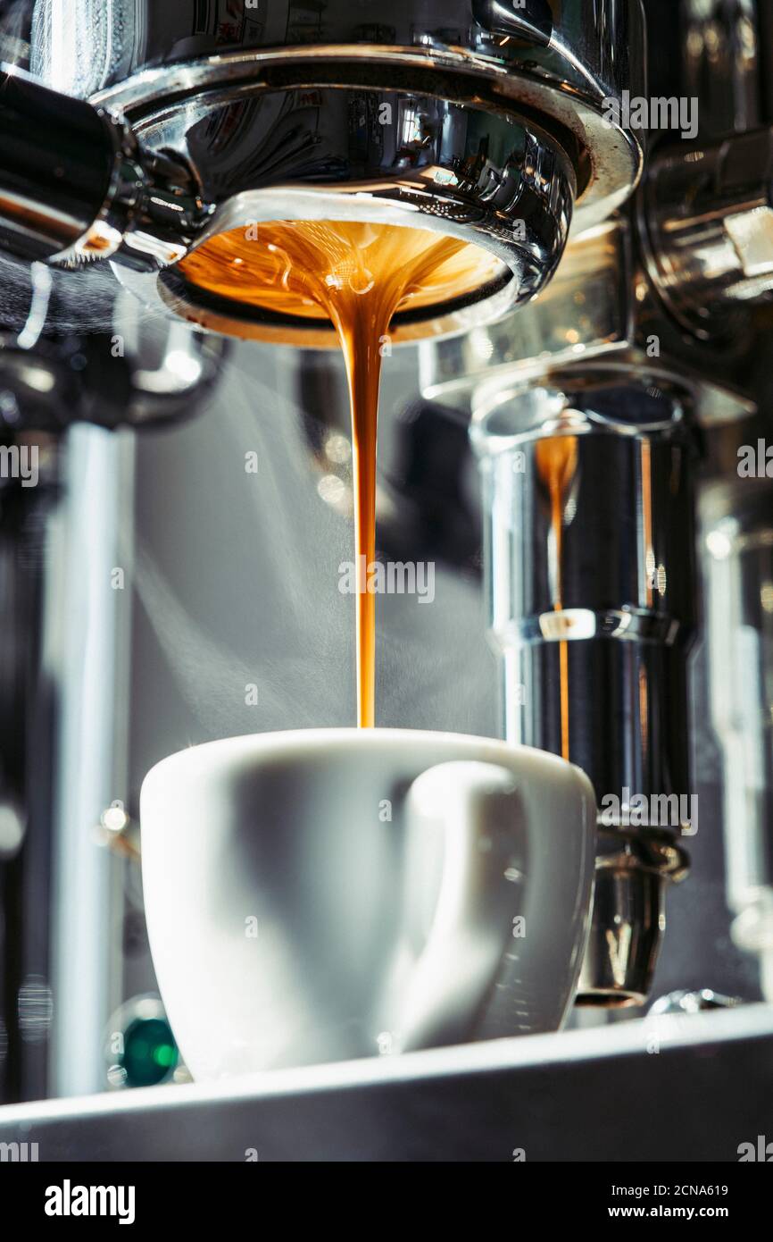 Espresso dripping from stainless steel portafilter into coffee cup ...