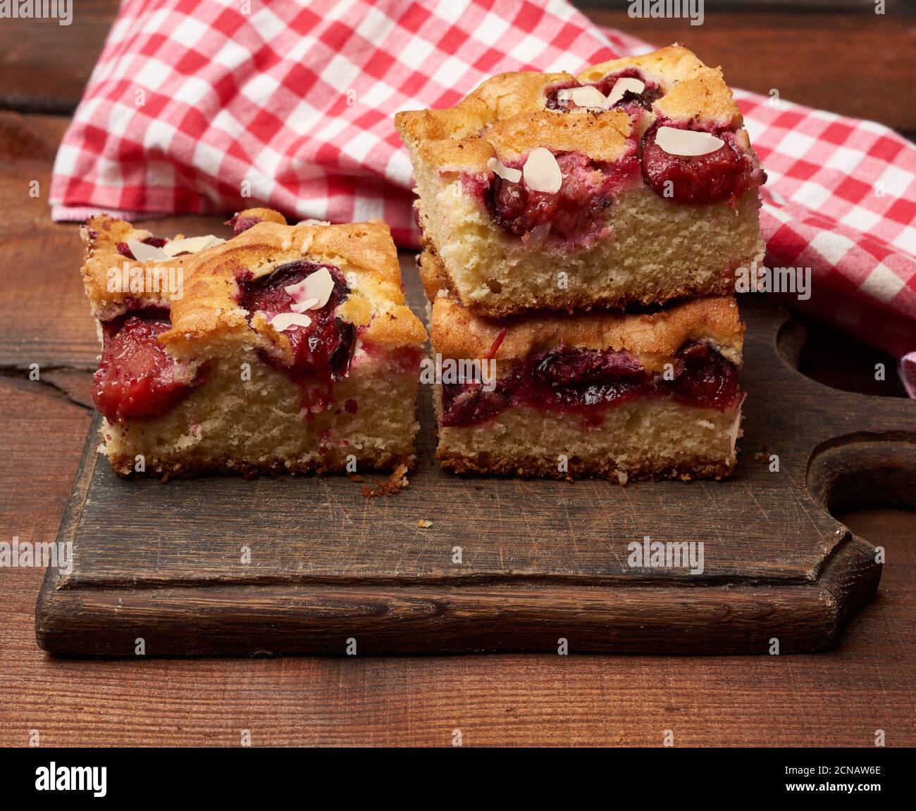 stack of square baked sponge cake slices with plums on wooden kitchen ...