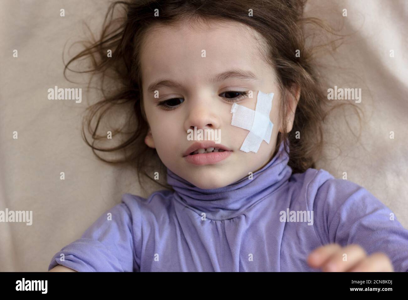Little kid girl after accident laying down with adhesive palter on face ...