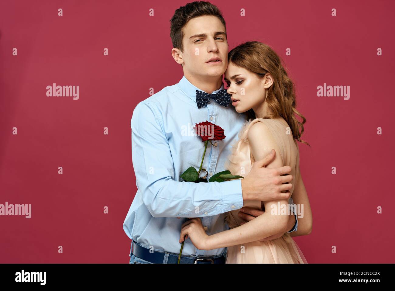 enamored man and woman with a red flower on a pink background hug each ...
