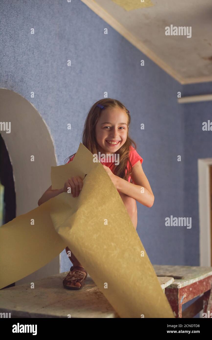 girl remove old wallpapers from wall. Girl helps to glue the wallpaper ...