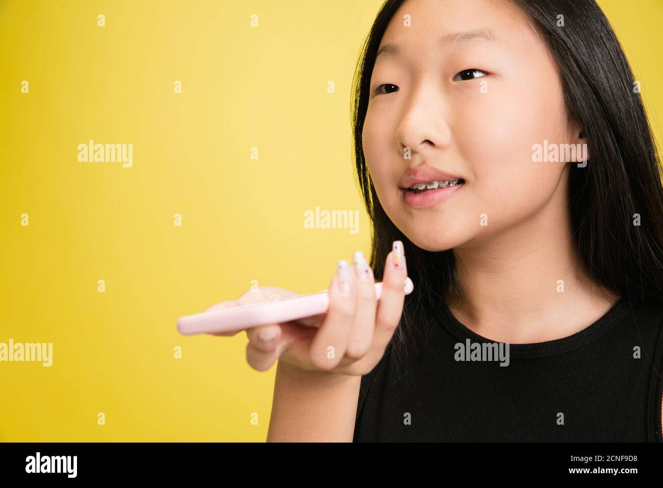 Recording message. Portrait of young asian girl isolated on yellow ...