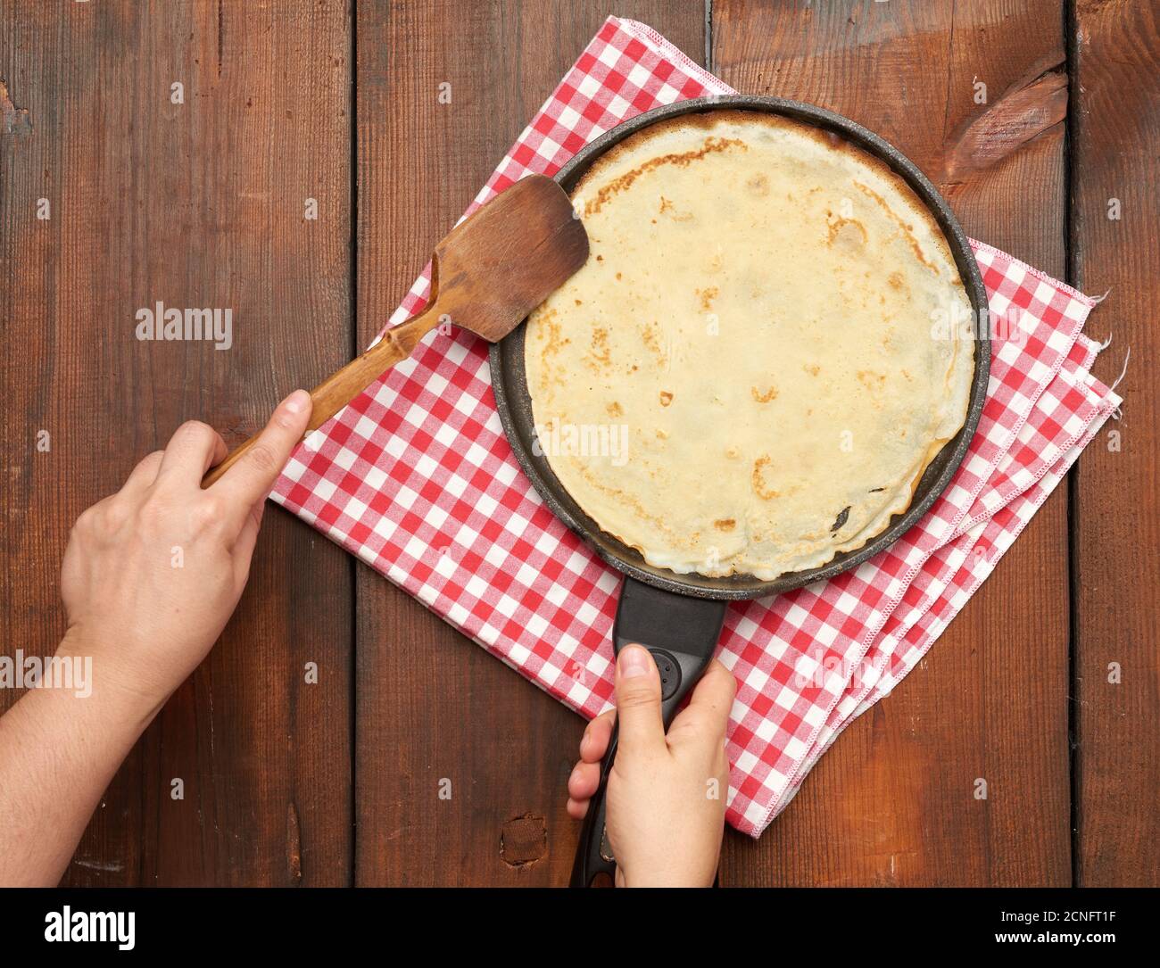 baked round big pancake in a black frying pan on a brown wooden table ...