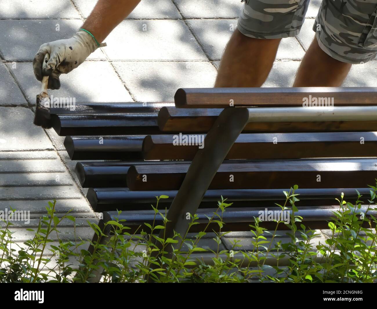 Man's hand holding a brush and painting a wooden bench with brown color ...