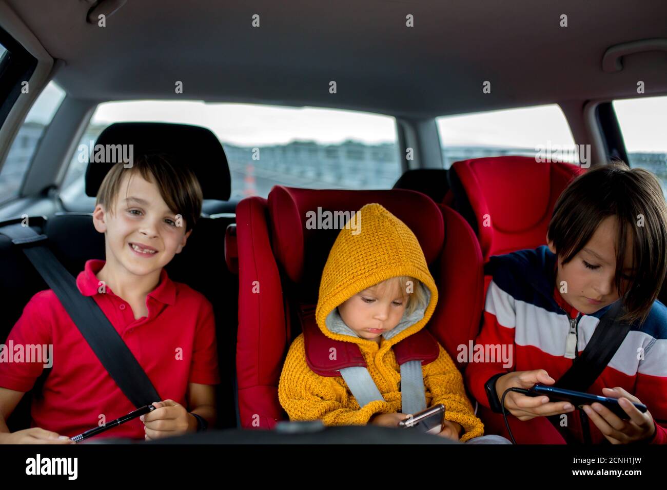 Three children, boys, traveling in car in carseat and playing on ...