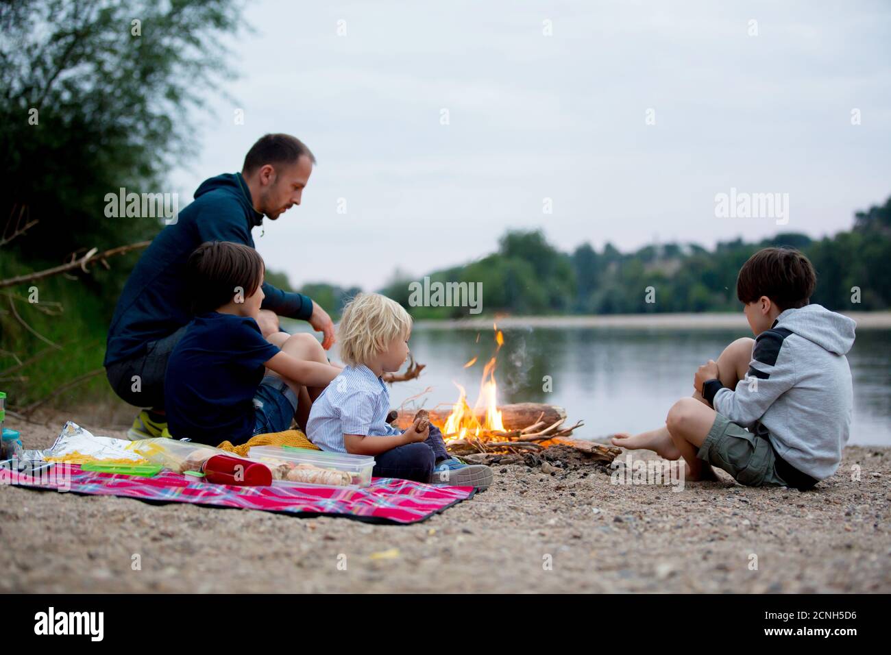 Family having picnic and campfire in the evening near river summertime ...