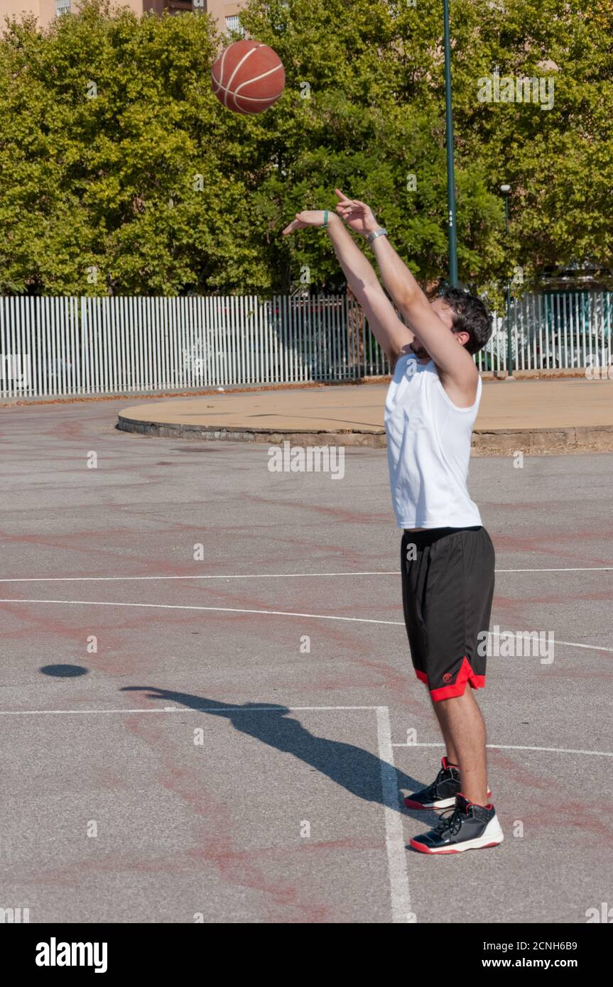Vertical shot of a young male playing basketball in a sports ground ...