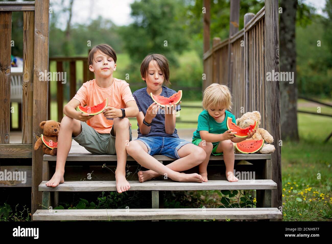 Three children, boy brothers, eating watermelon, sitting on stairs ...