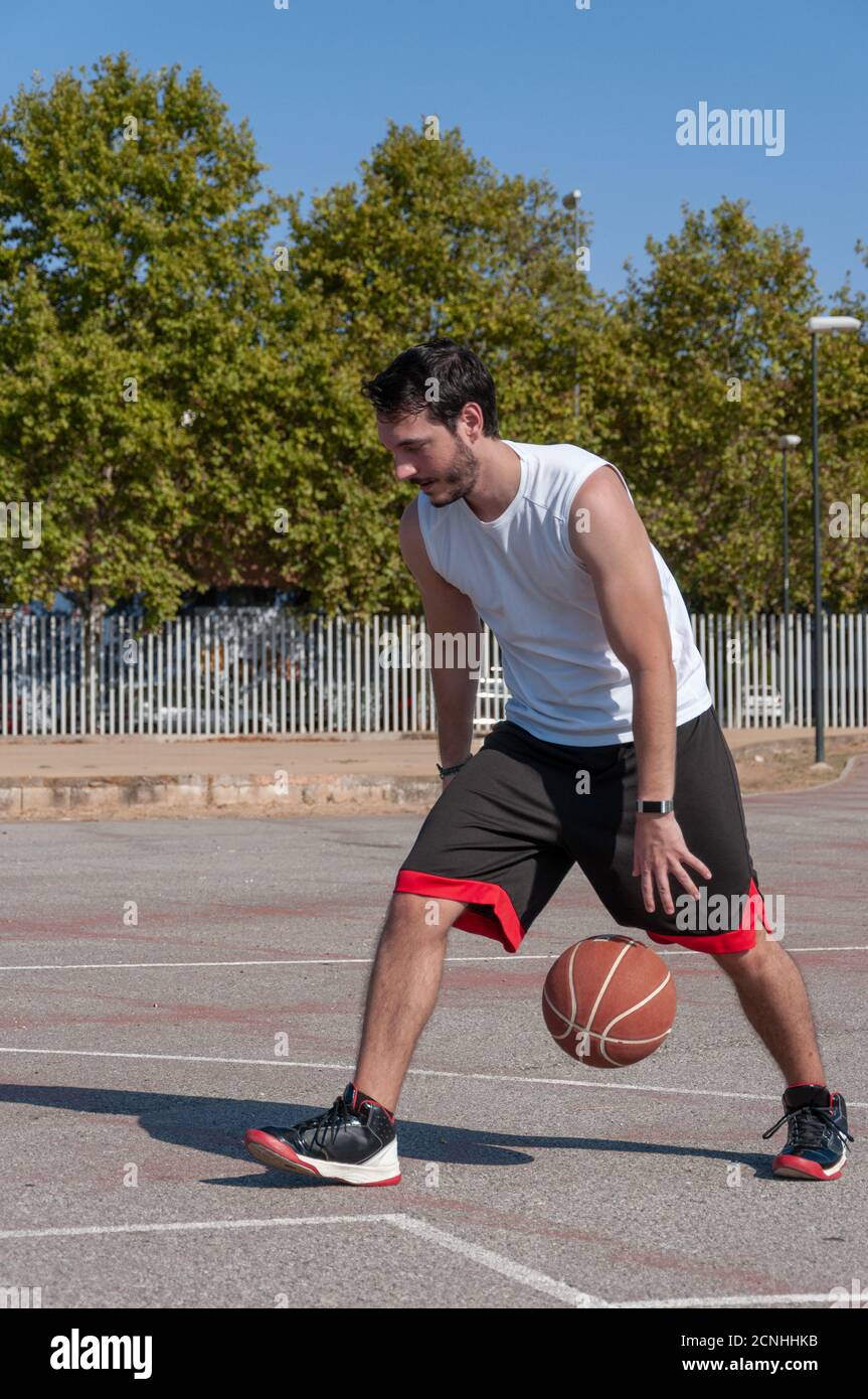 Vertical shot of a young male playing basketball in a sports ground ...