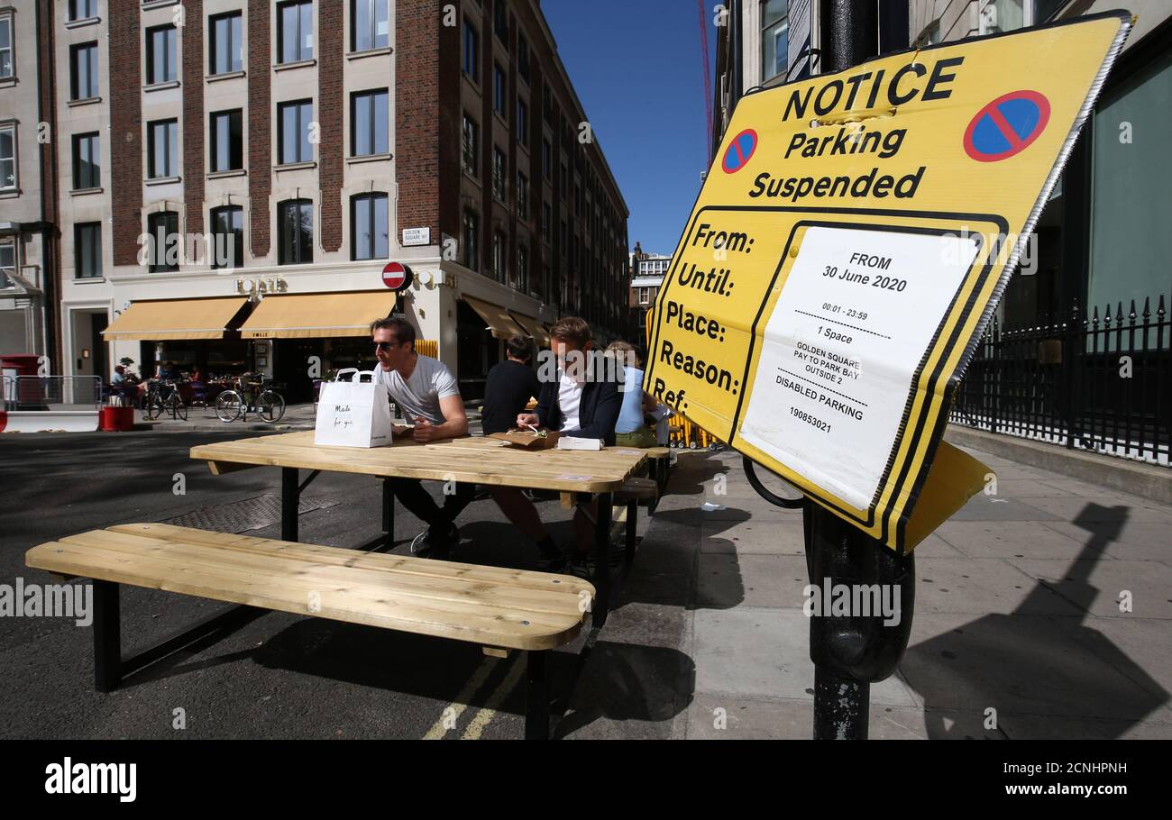 People eat lunch at tables and benches placed in the roadway adjacent ...