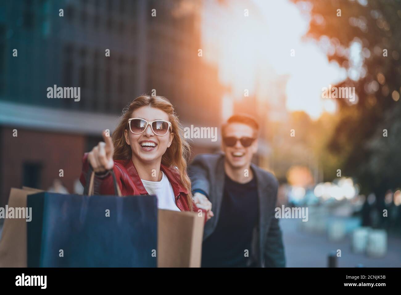Front view of a casual couple of shoppers running in the street towards ...