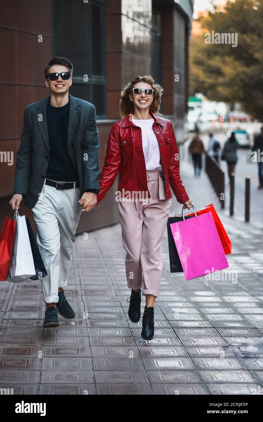 Front view of a casual couple of shoppers running in the street towards ...
