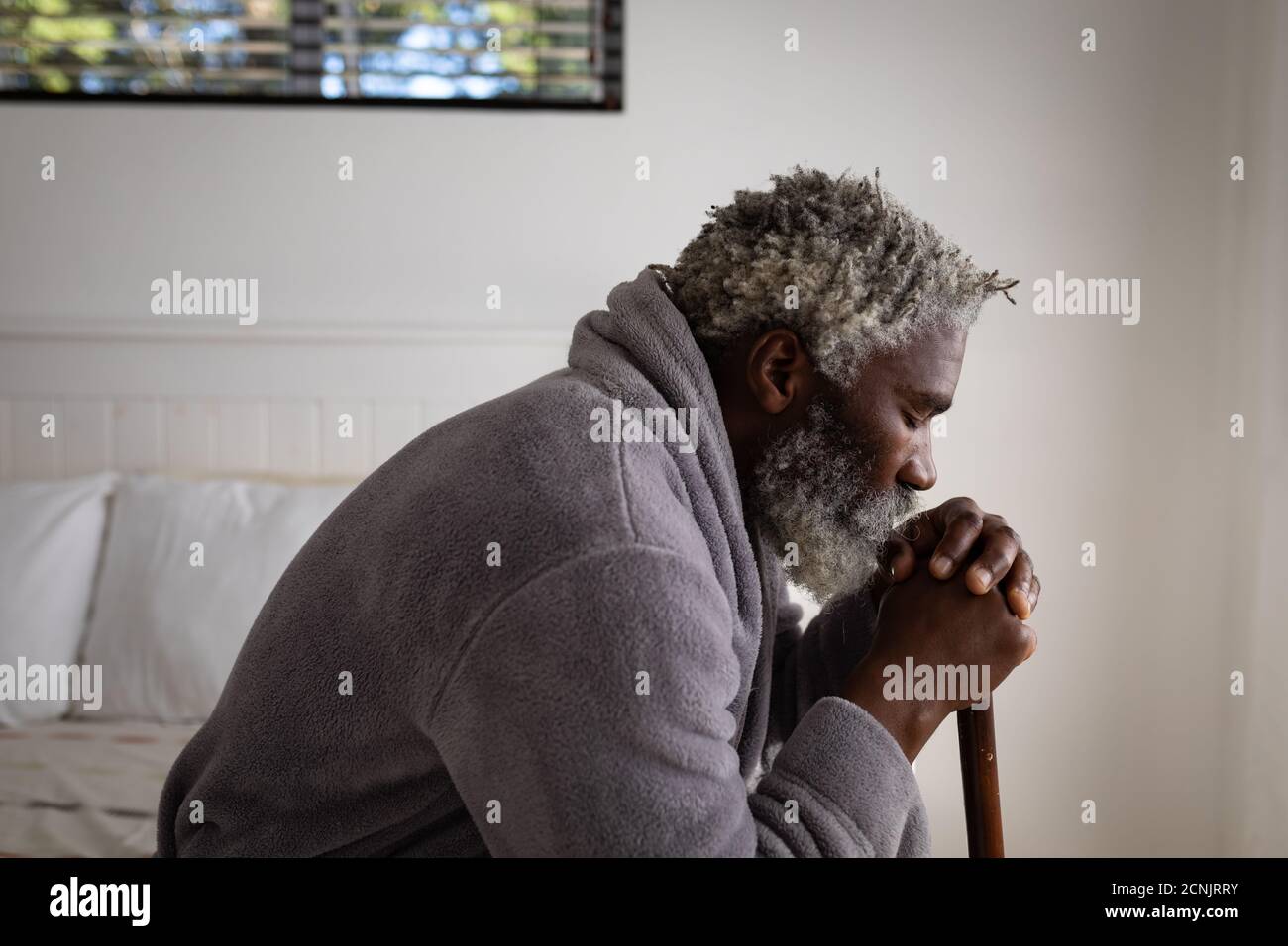 African American senior man sitting on a bed in a bedroom, resting his ...