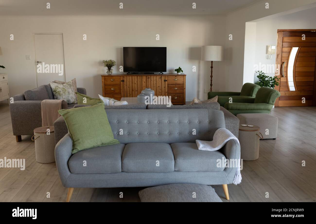 Modern, empty living room with two grey and one green couches, a big tv ...