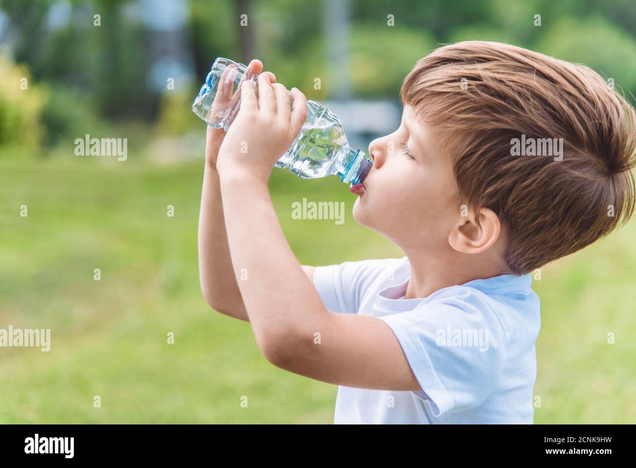 Handsome boy drinks clean water from a bottle on the street in summer ...