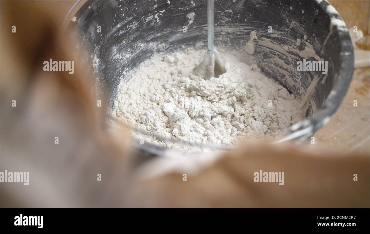 The worker mixes the mixer with plaster in a bucket with water to level ...