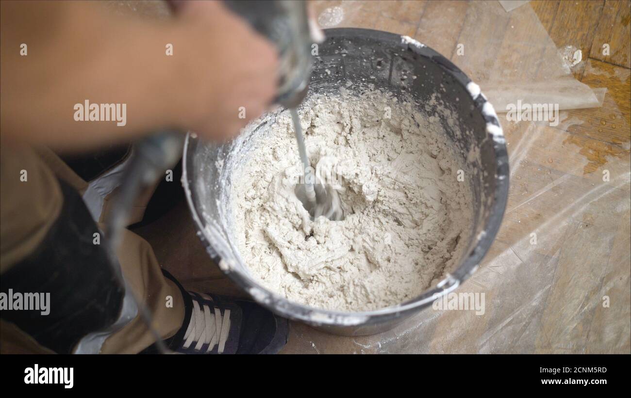 The worker mixes the mixer with plaster in a bucket with water to level ...