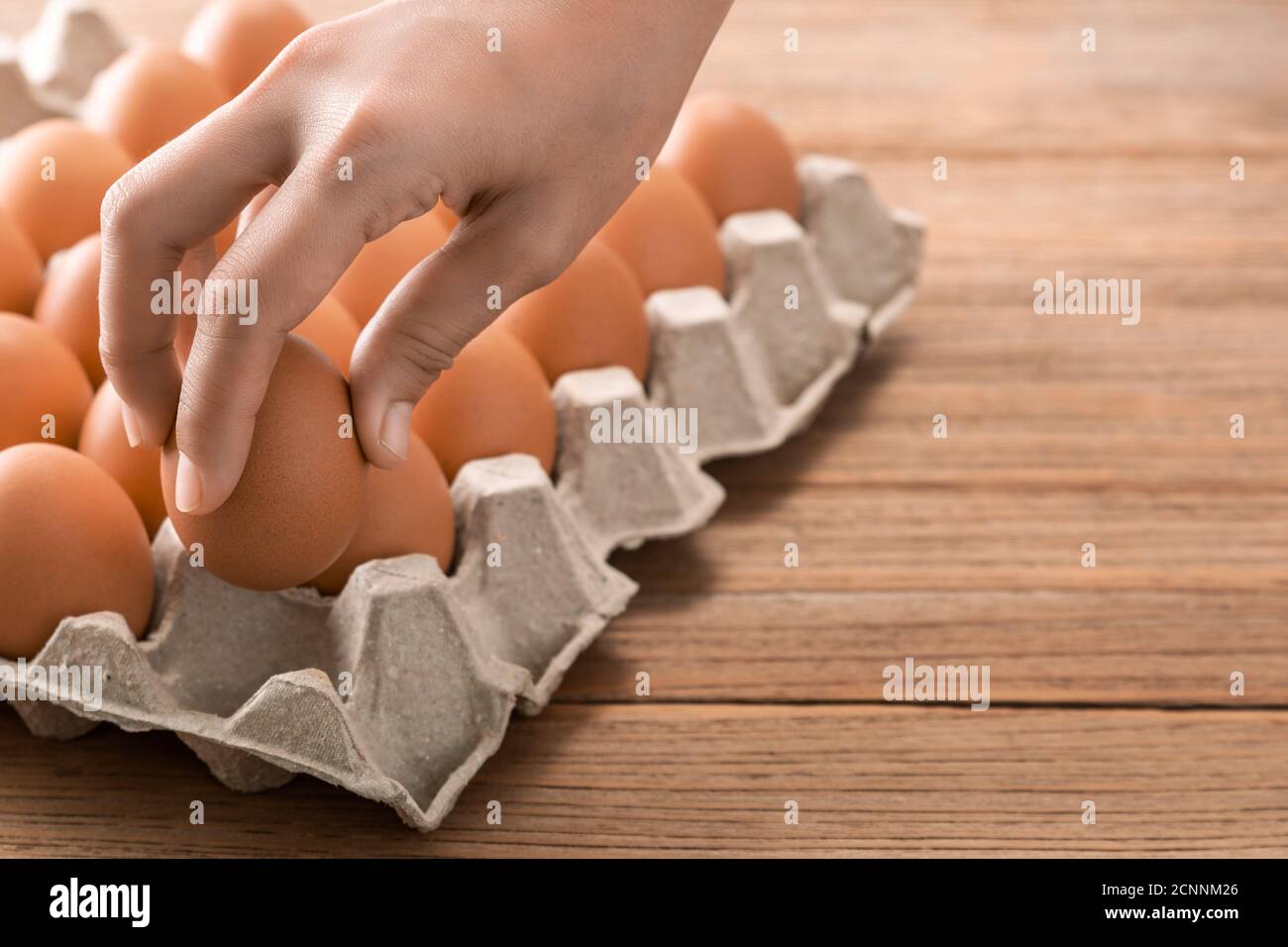 Women's hand taking hen's brown egg from many fresh raw brown chicken ...