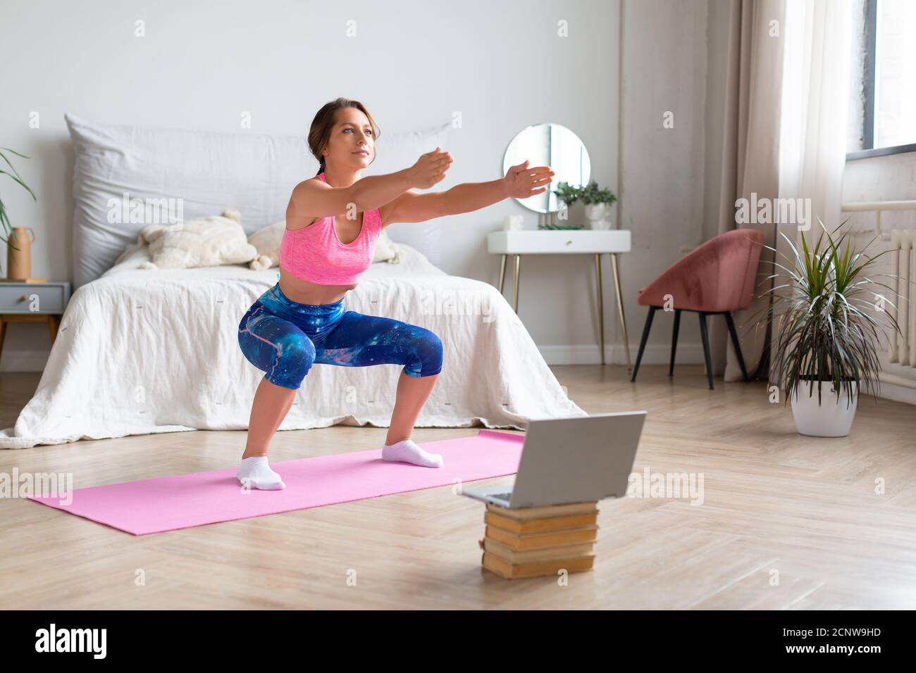Woman squatting at home in front of laptop. Healthy lifestyle concept ...