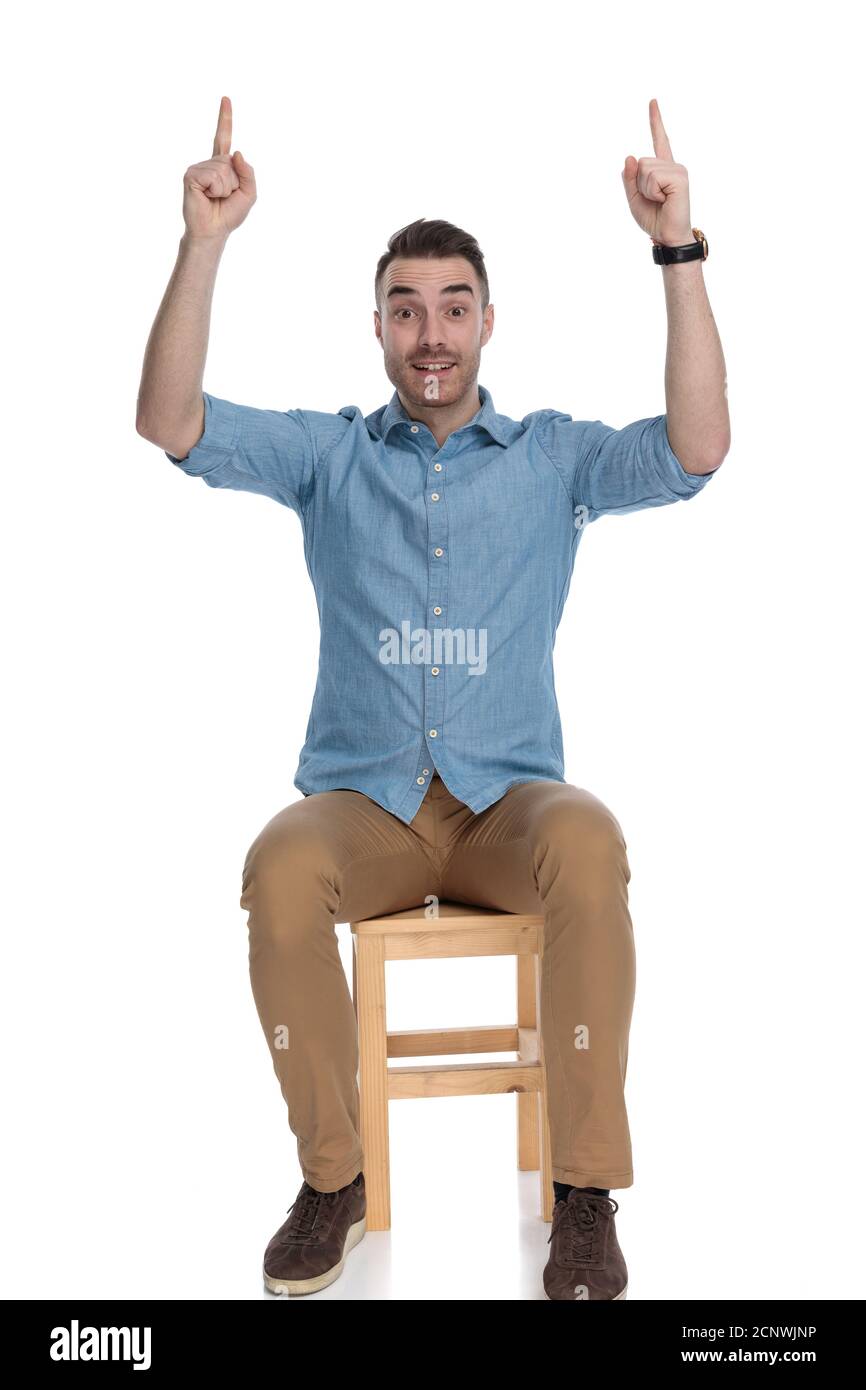 Positive smart casual man pointing up with both hands while sitting on ...