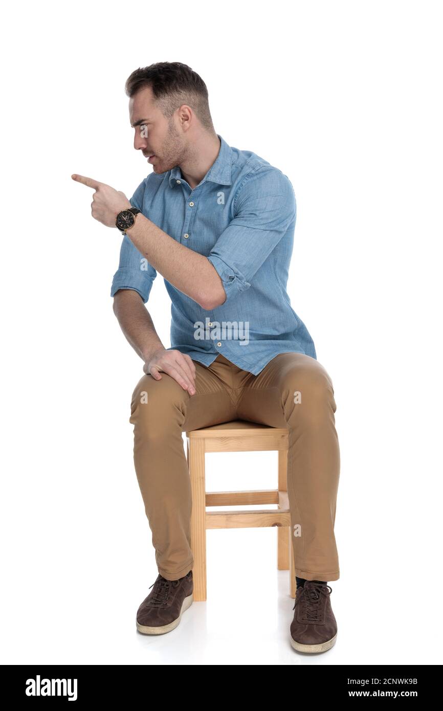 Angry smart casual man frowning and pointing while sitting on a chair ...